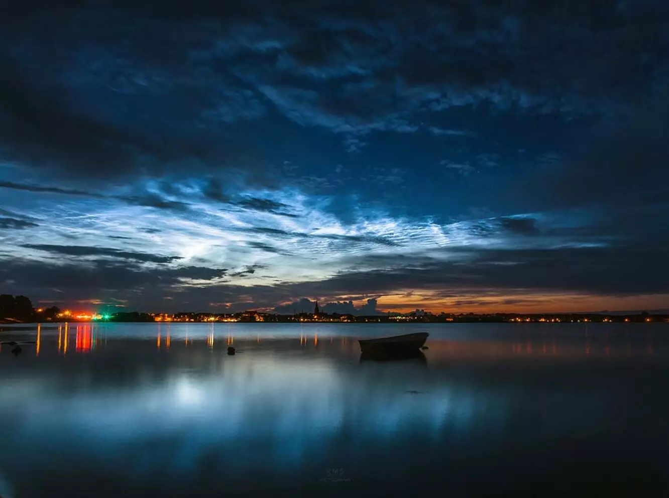 Awan putih dan biru yang menakjubkan dengan cahaya latar keperakan menari-nari di atas kota Nykøbing Mors di Denmark saat fajar pada tanggal 1 Juli.