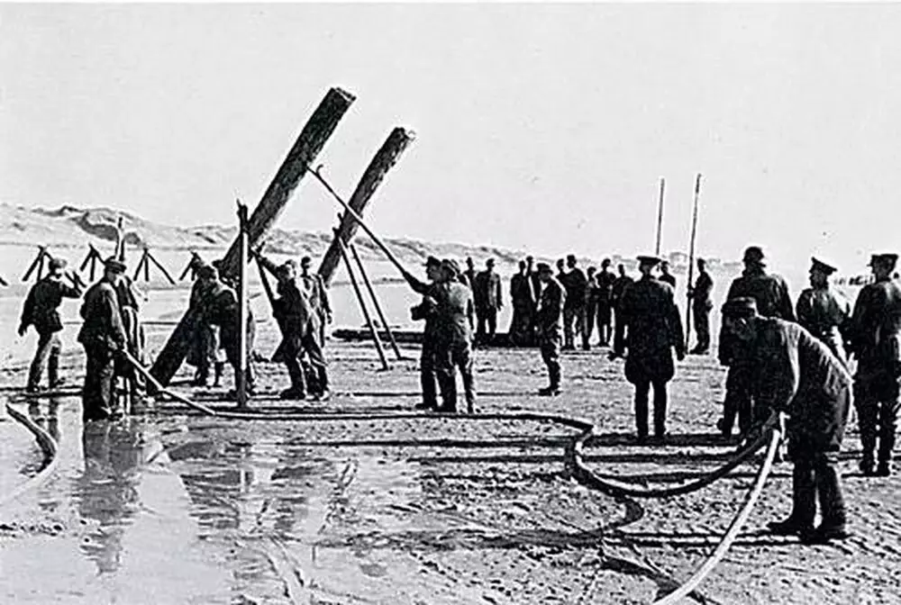 La construction du mur de l'Atlantique bat son plein. Derrière les rondins inclinés, on distingue une série d'obstacles en forme de tétraèdres.