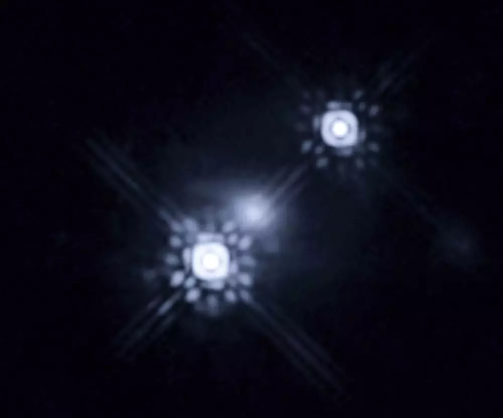 Imagen del Hubble que muestra el cuásar HE 1104-1805 duplicado como resultado de la lente gravitatoria de una galaxia ubicada entre él y nosotros (es visible como una nube más tenue alrededor de los reflejos brillantes del cuásar)